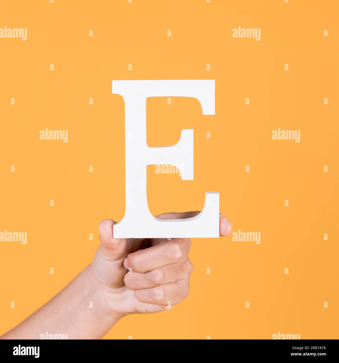 Close up hand holding up uppercase capital letter e yellow background ...