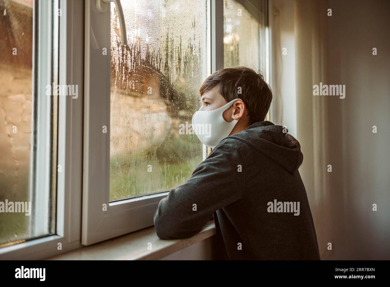 Sideways boy with face mask looking through window Stock Photo - Alamy