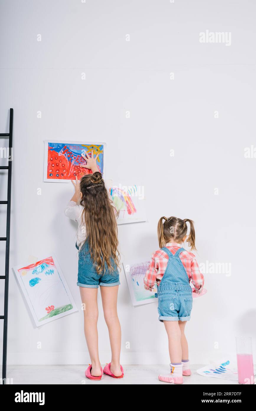Little girls hanging drawings white wall Stock Photo - Alamy