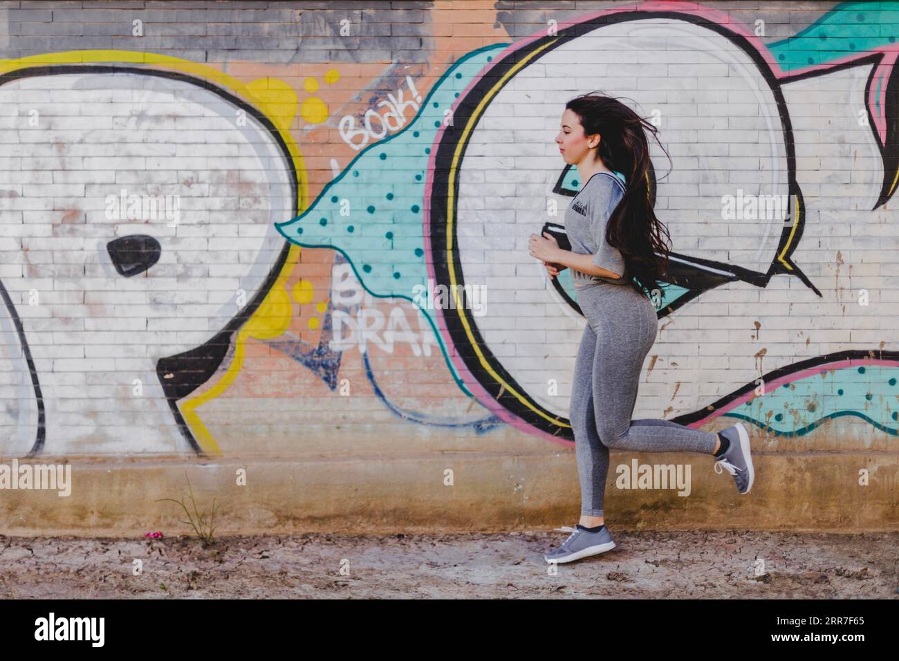Brunette woman running against concrete wall Stock Photo - Alamy