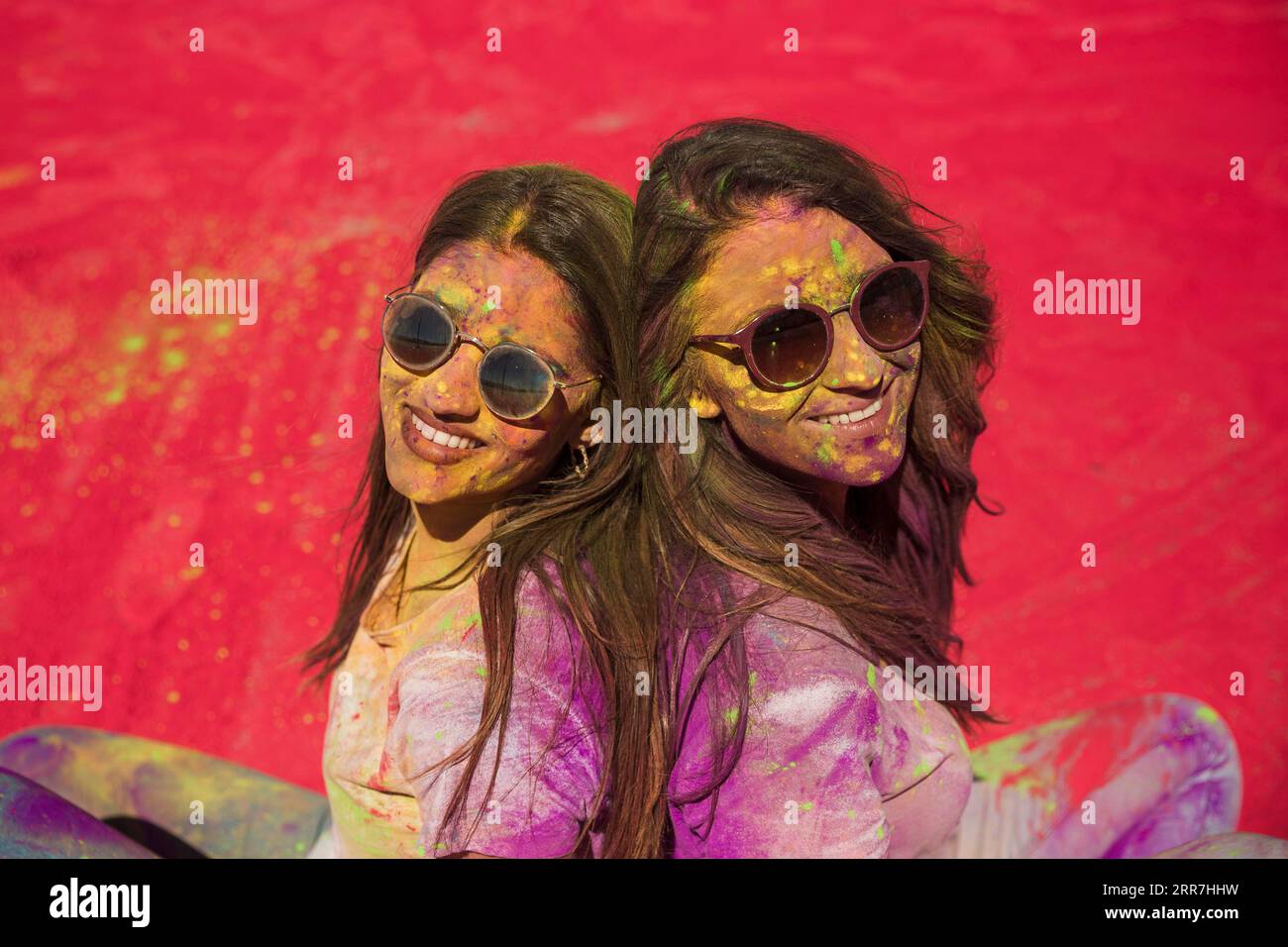 Two happy young women covered with holi color sitting back back Stock ...