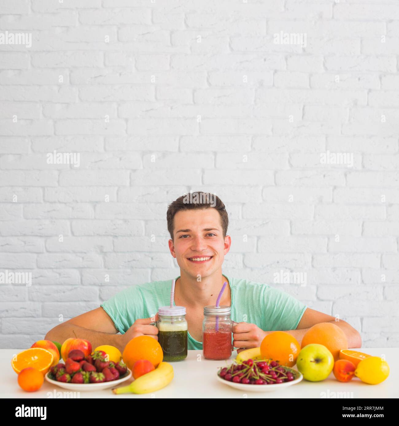 Happy young man holding smoothies with colorful fresh organic fruits ...