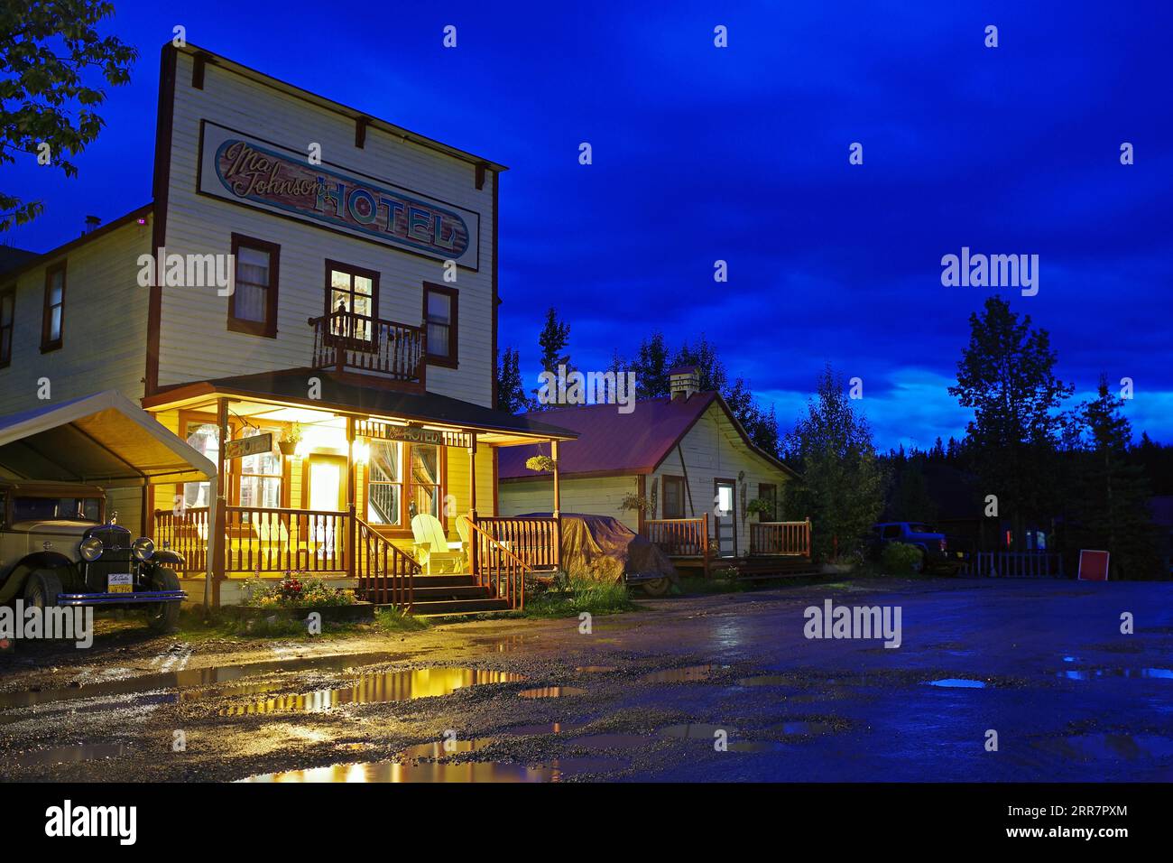 Evening illuminated facade of an old hotel, wooden house, vintage car ...