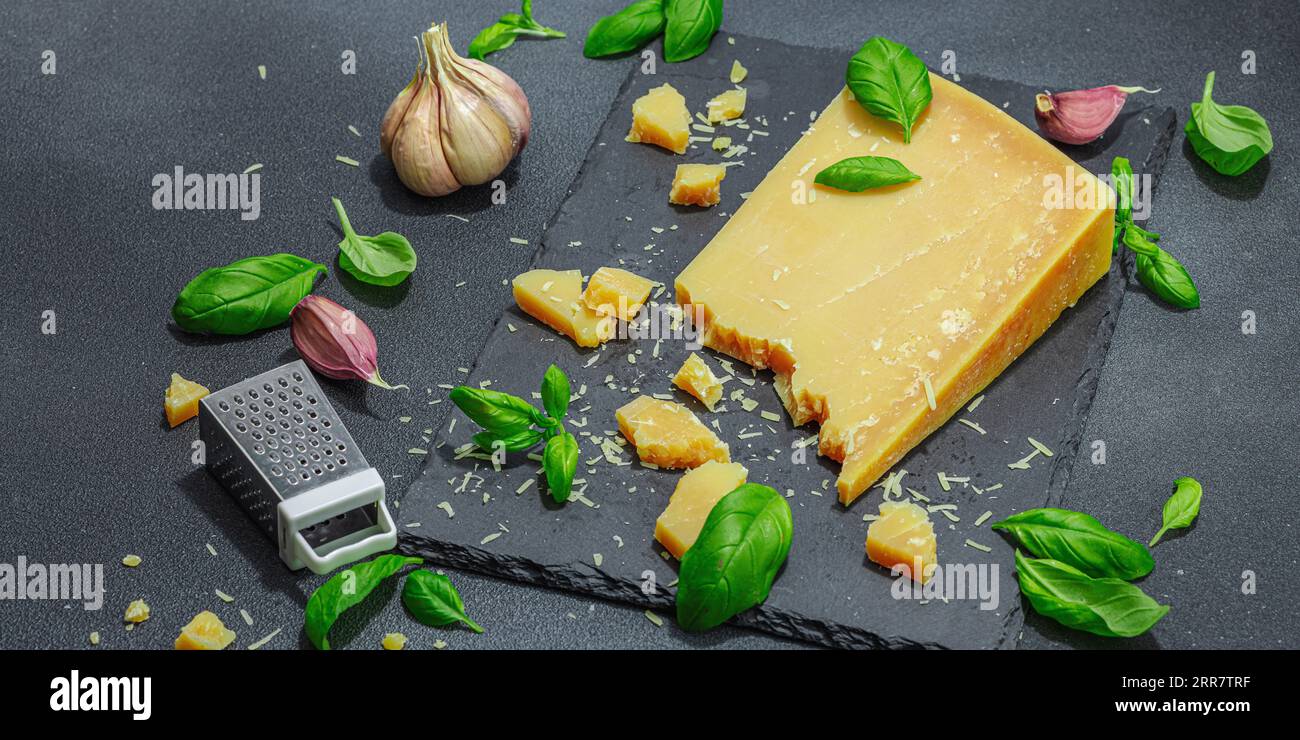 Piece of Parmesan cheese on modern stand. Garlic, fresh basil leaves ...