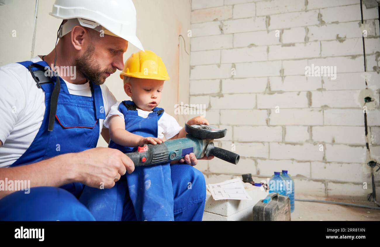 Little boy sitting on father lap and holding electric power grinding ...