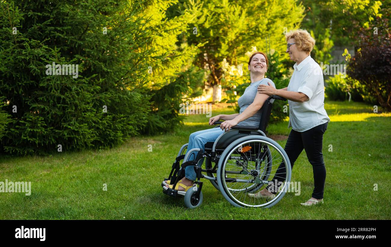An elderly woman is carrying an adult daughter sitting in a wheelchair ...