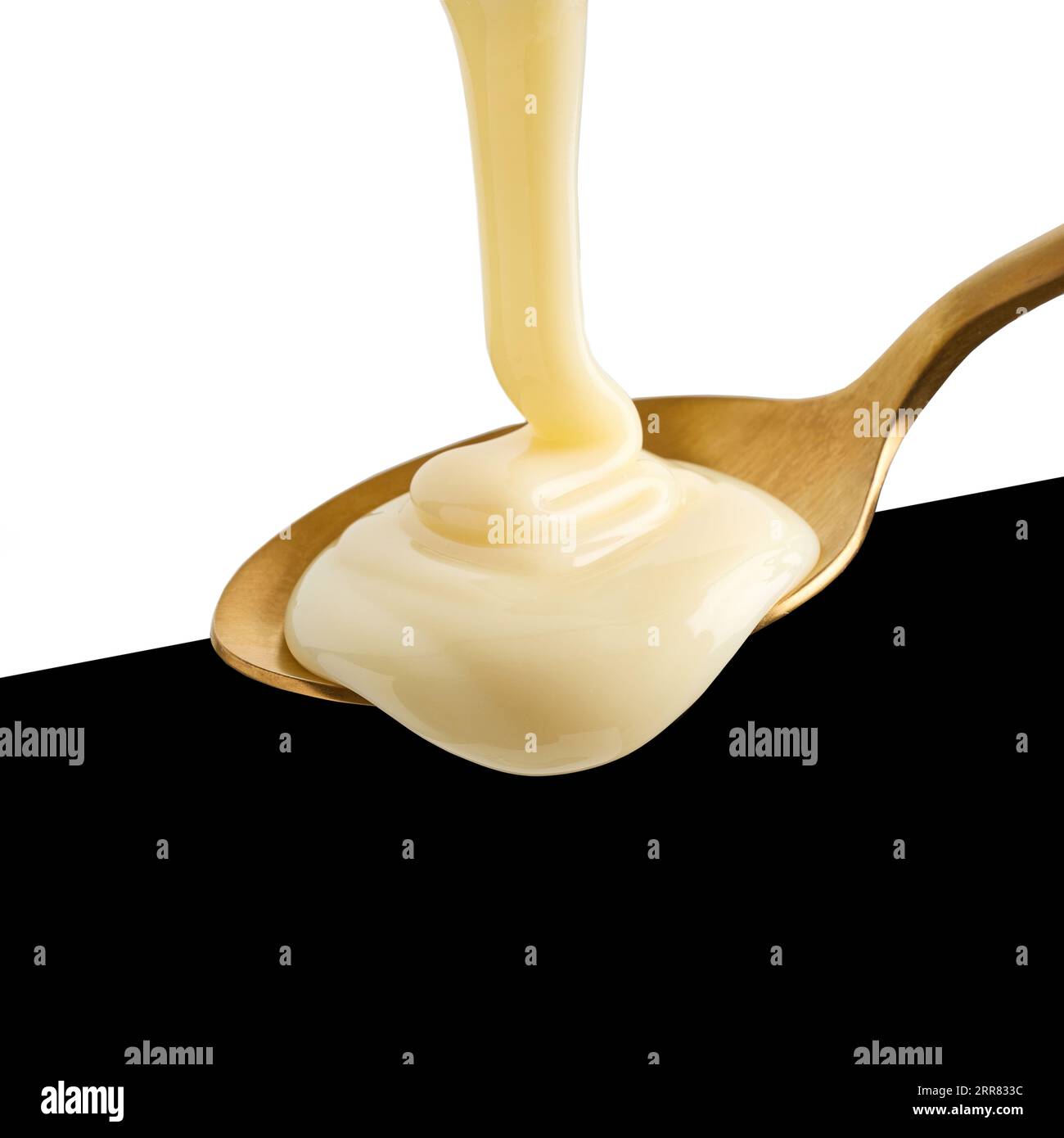 condensed milk pouring into golden spoon isolated on black and white ...