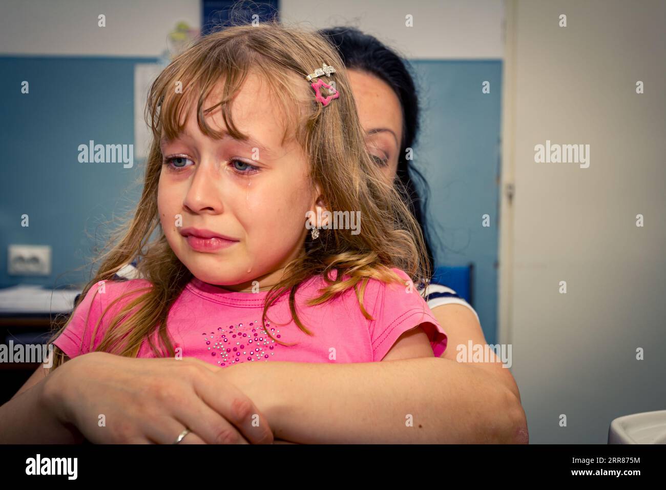 Preschooler, scared and crying cute little child is sitting on mom's ...