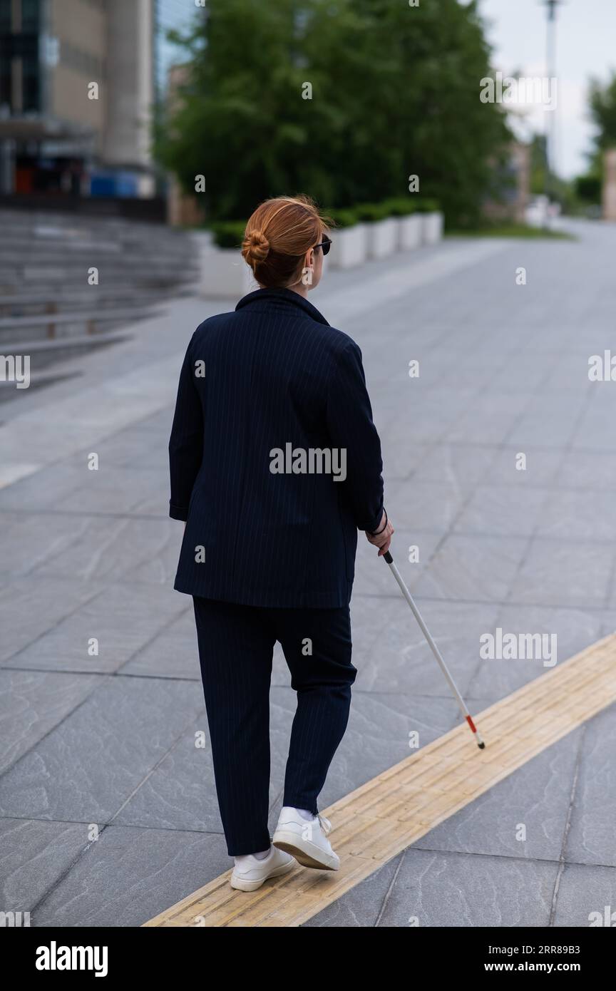 Blind businesswoman walking along tactile tiles with a cane Stock Photo ...