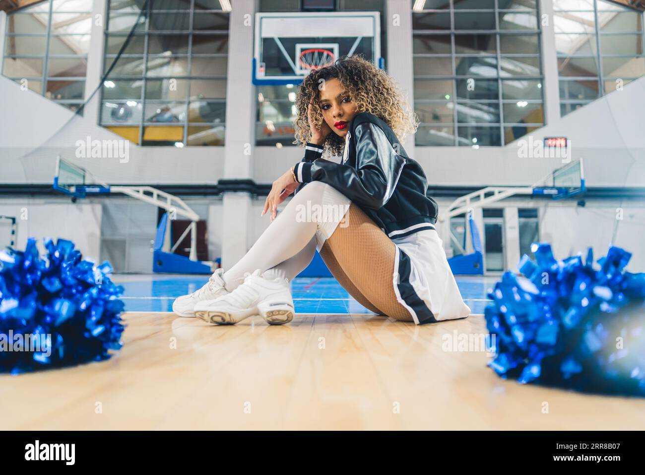 Cheerleader woman with afro hair sitting on a basketball court floor ...