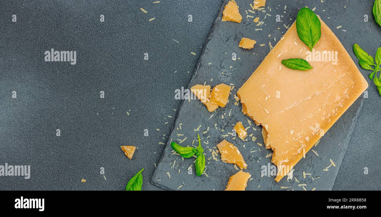 Piece of Parmesan cheese on modern stand. Garlic, fresh basil leaves ...