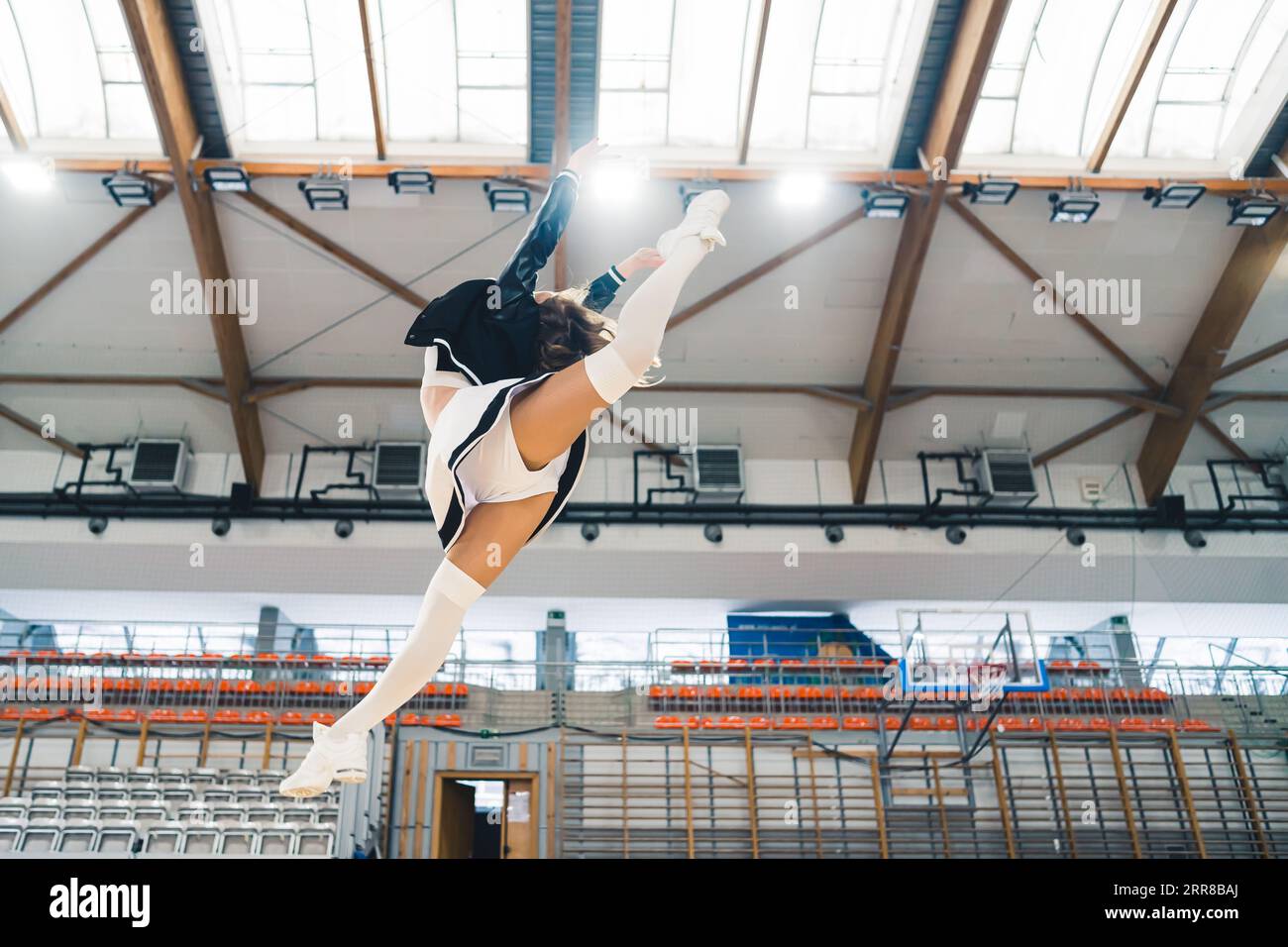 Cheerleader woman doiong a jump split in the air indoor on a sport ...