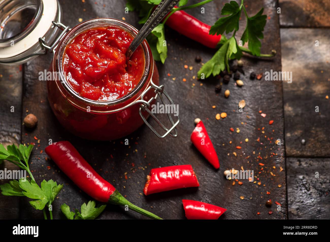 Spicy homemade chili sauce in a small glass jar on a dark wooden ...
