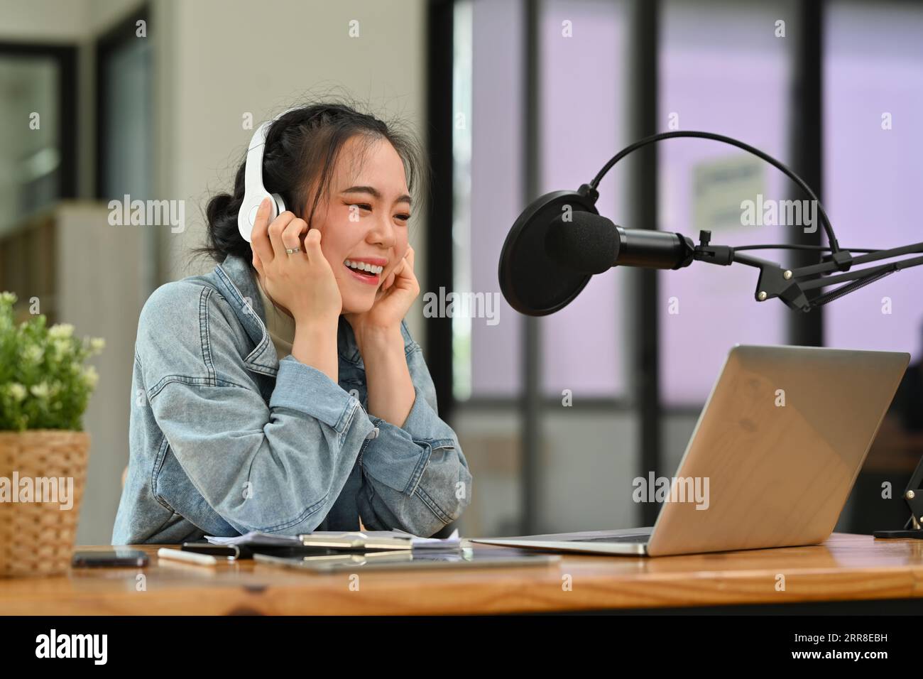 Cheerful female podcaster wearing headphone talking into a microphone ...