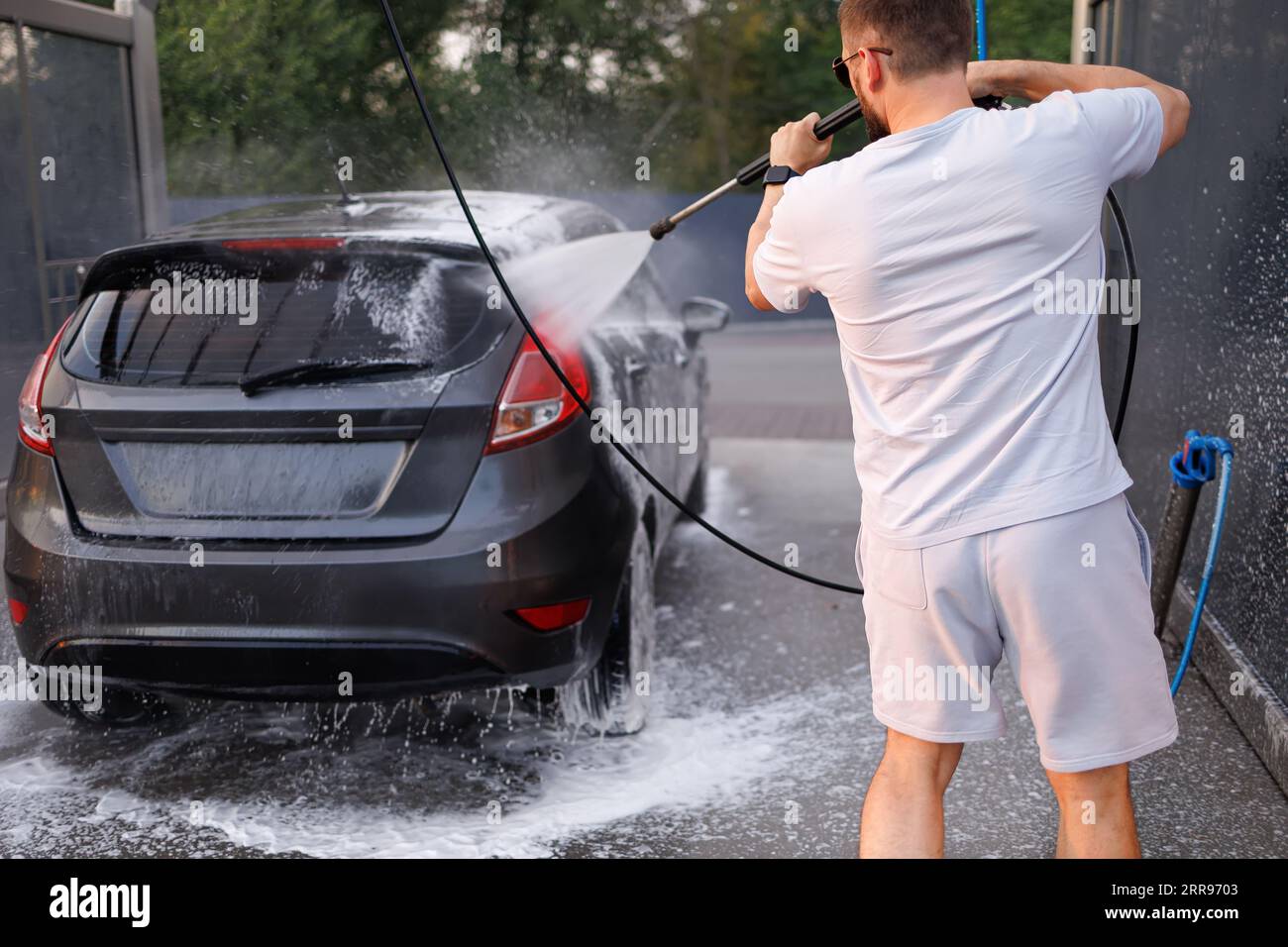 A man stands back and washes the back of the car with a water cannon. A ...