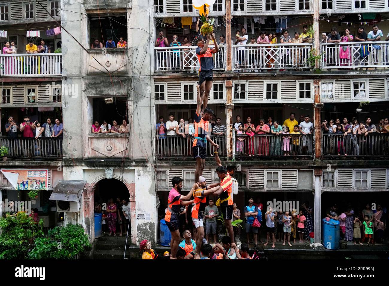 Revelers form human pyramids to reach an overhanging earthen pot while ...