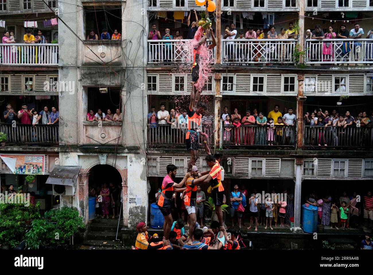 Revelers form human pyramids to reach an overhanging earthen pot while ...