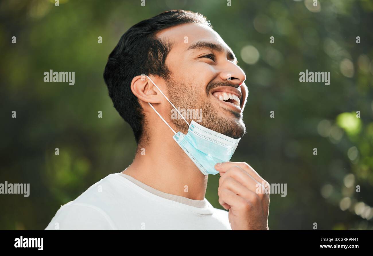Smile, mask and remove with a man breathing fresh air in nature ...