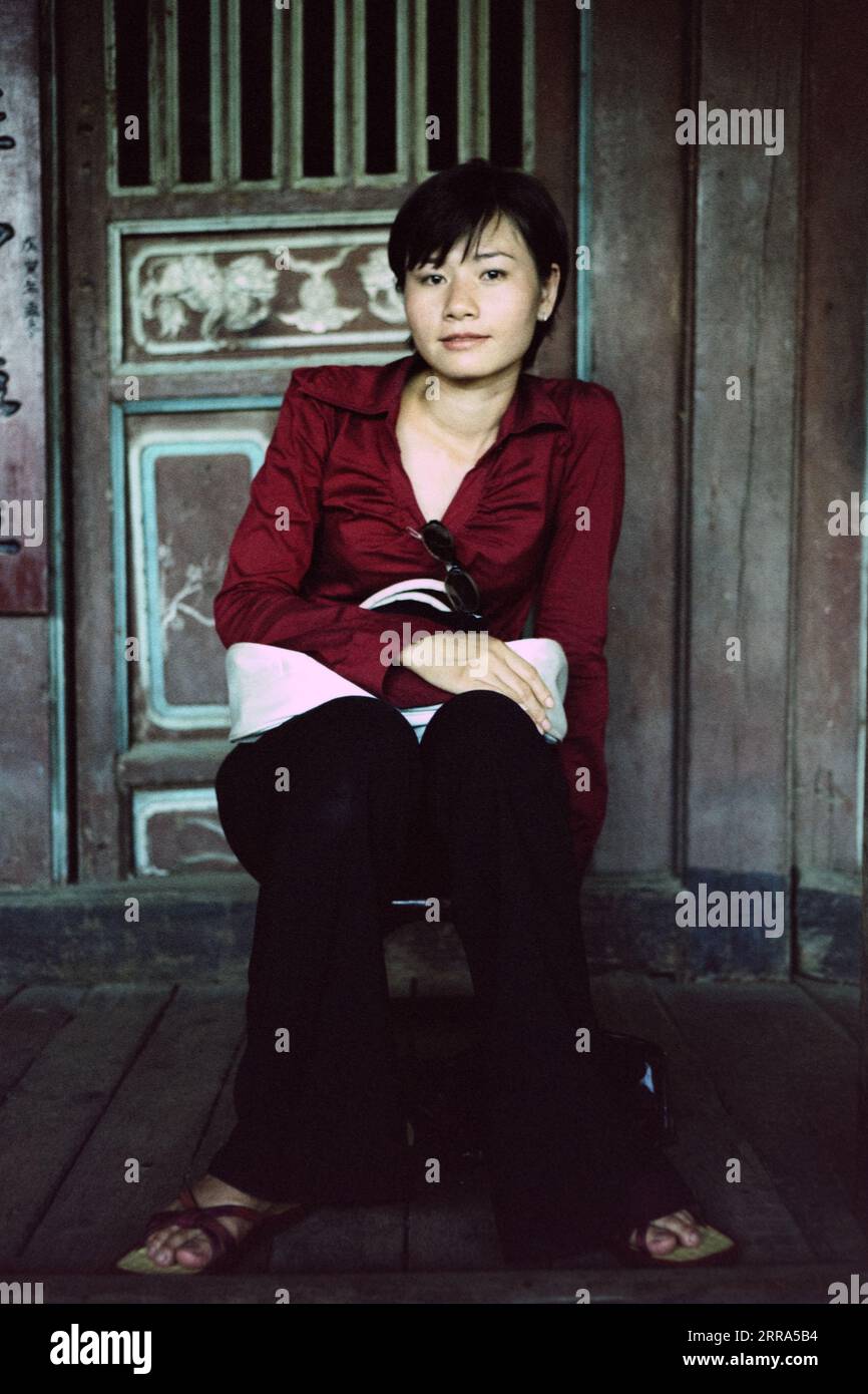 Portrait of a young Vietnamese woman sitting on a chair dressed up ...