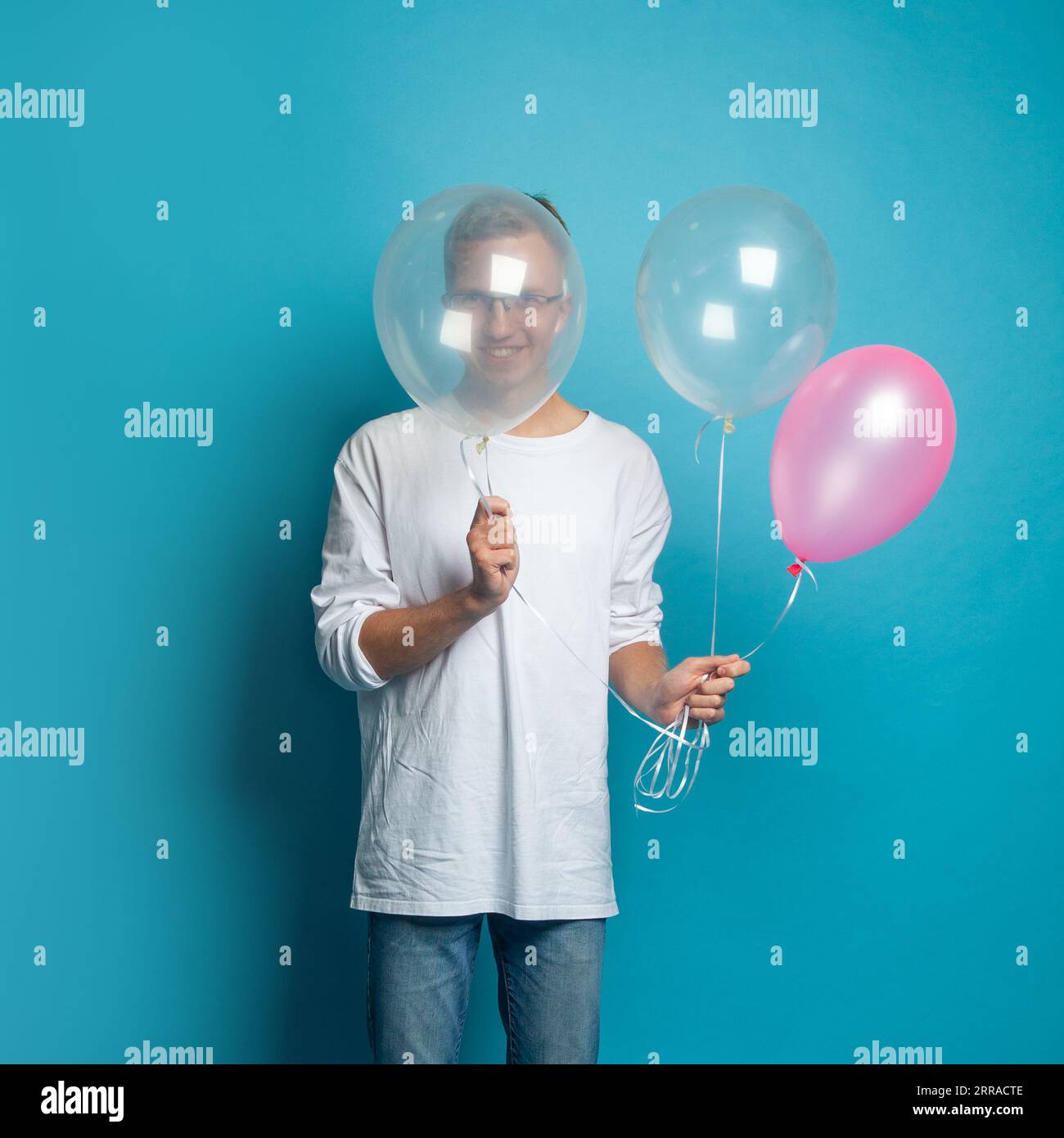 Happy young man hiding his face behind balloon against colorful blue ...