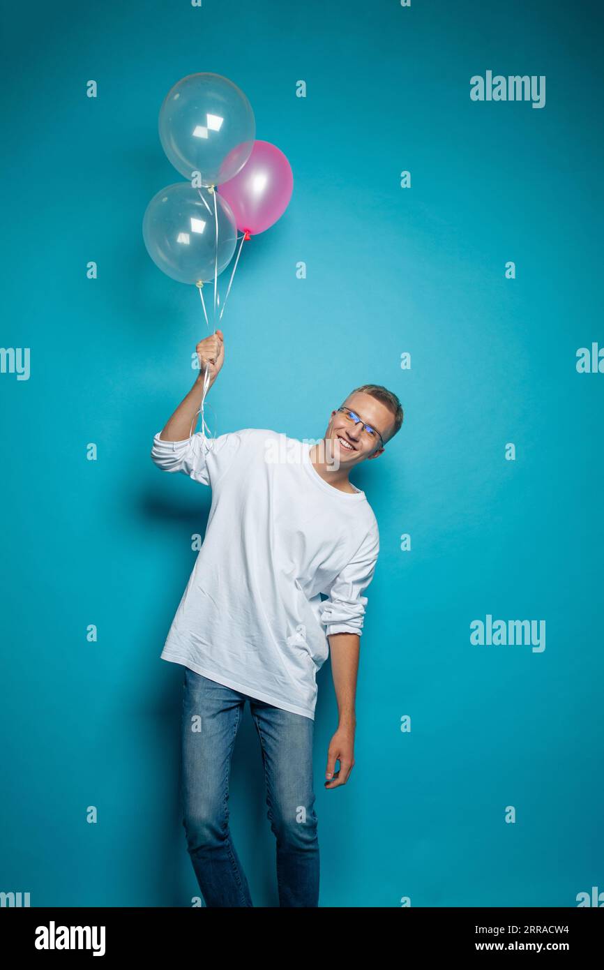 Surprised man with balloon standing against colorful blue studio wall ...