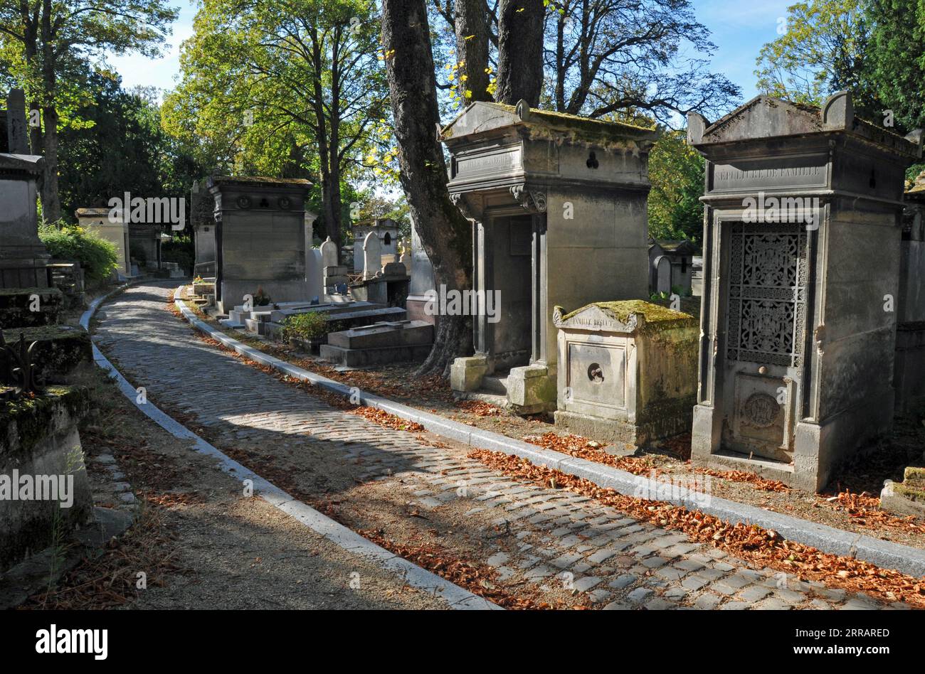 A cobblestone walkway curves past old tombs and moss-covered grave ...