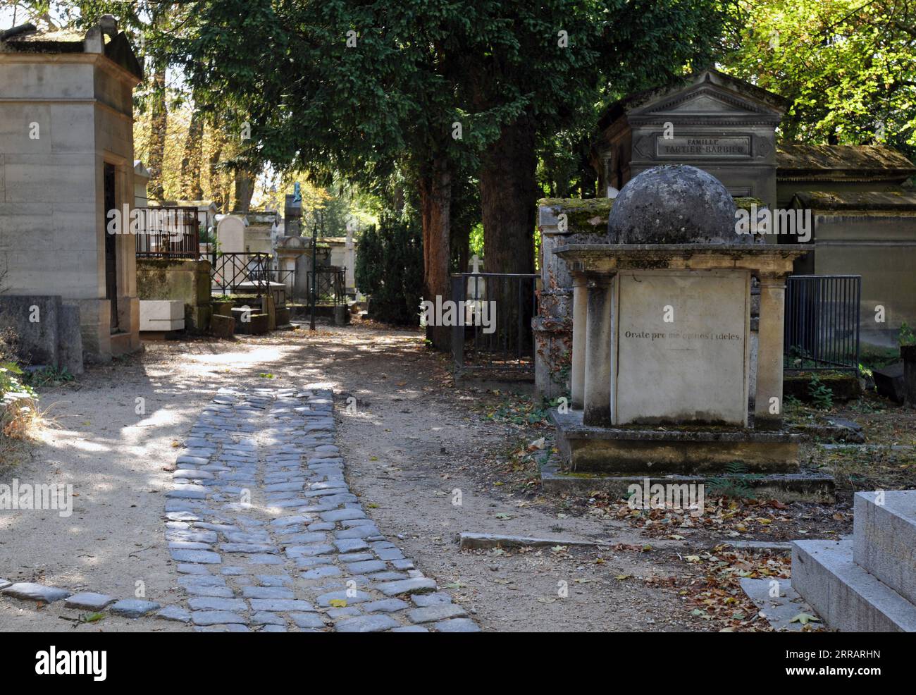 A tree-lined cobblestone walkway leads past old tombs and grave sites ...