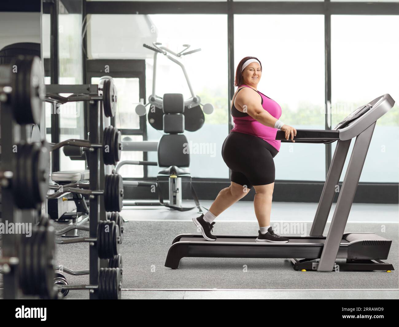 Smiling young overweight woman walking on a treadmill at the gym Stock ...