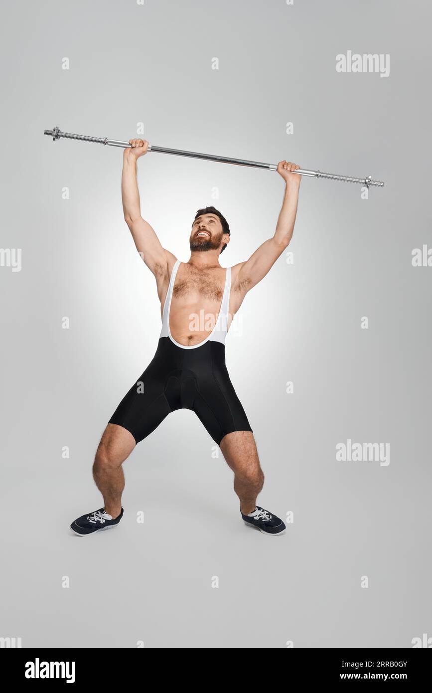 Muscular man in sportswear lifting unweighted barbell in studio. Full ...