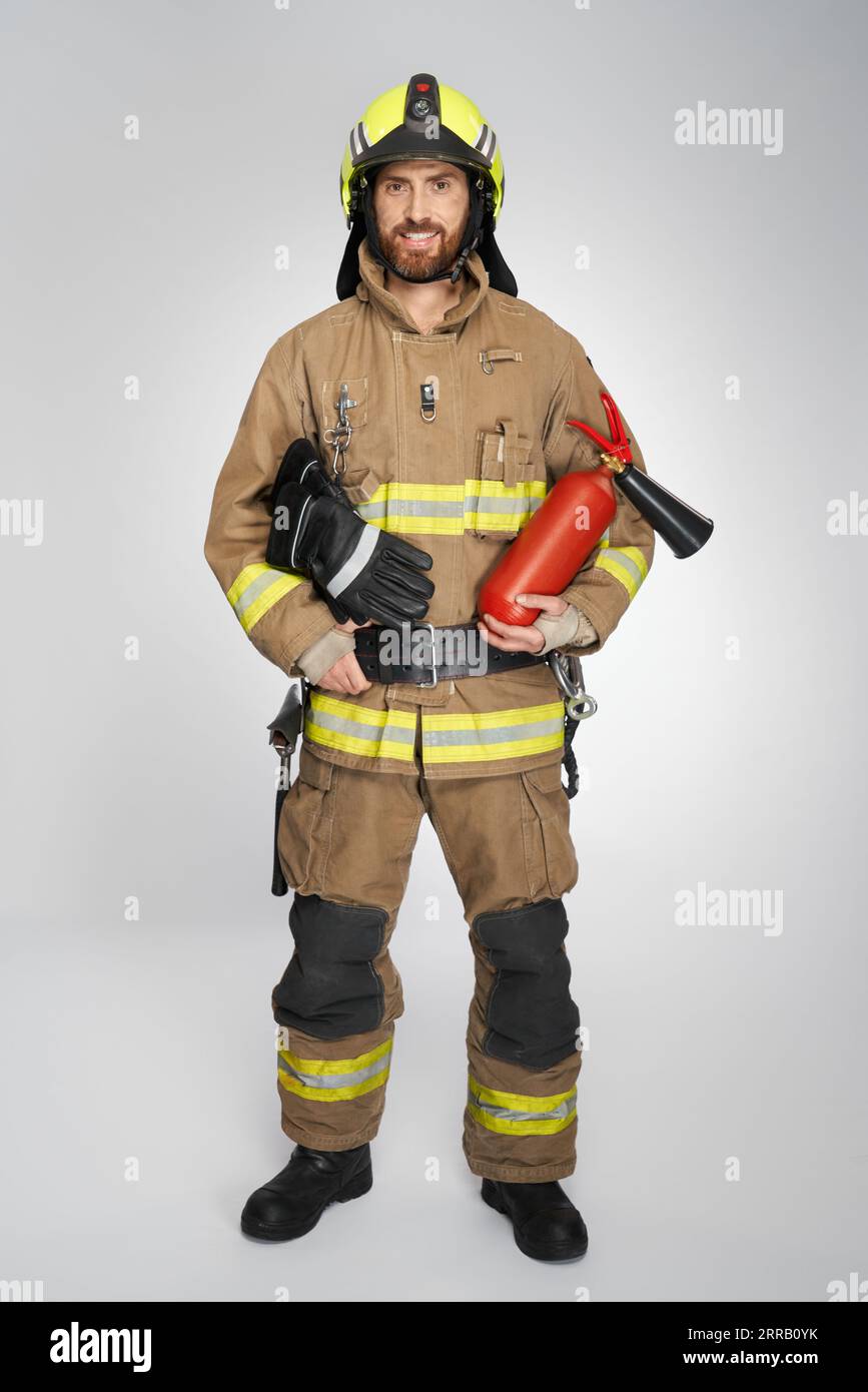 Young firefighter in helmet holding fire extinguisher in studio. Front ...