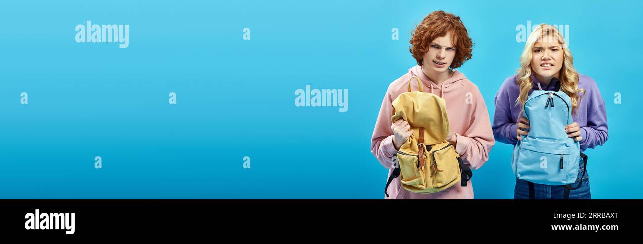 irritated teenage classmates in holding school backpacks and looking at ...