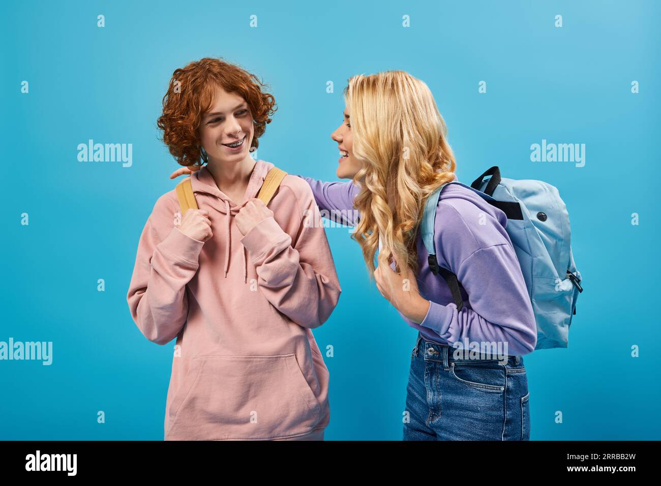 blonde teen girl with school backpack embracing smiling redhead ...