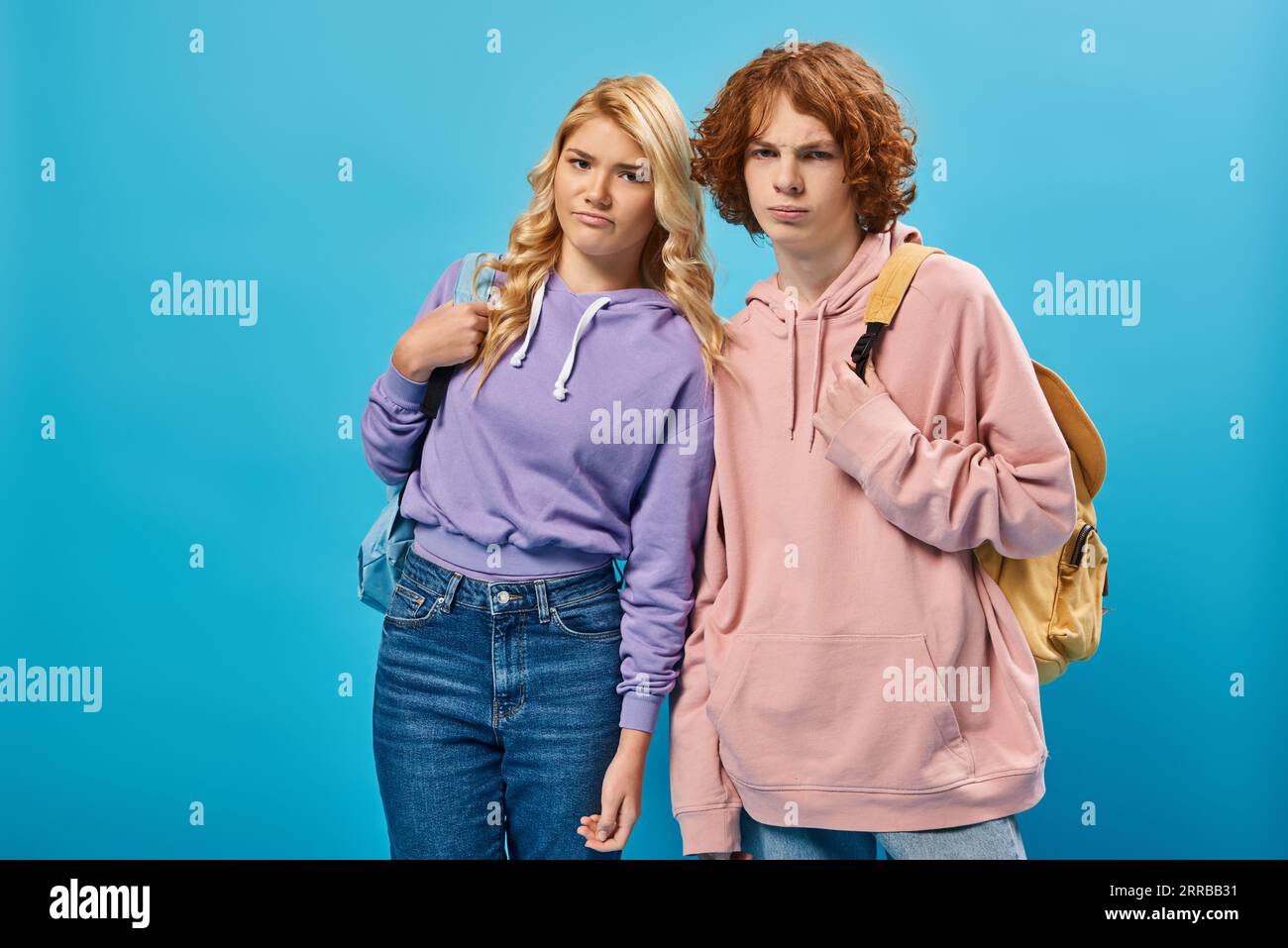 displeased teenage classmates standing with school backpacks and ...