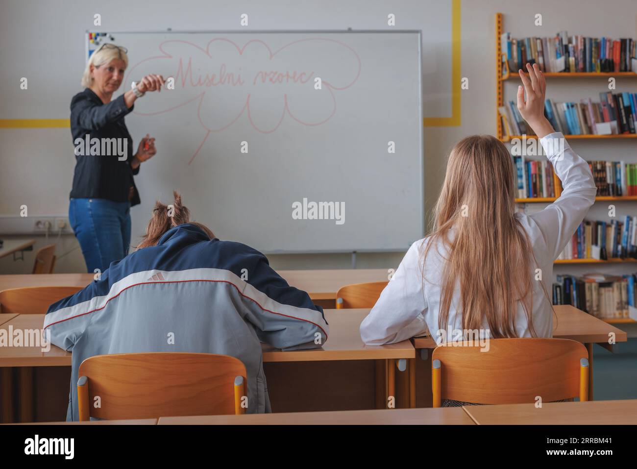 Girl student writes down notes and raises her hand while a female ...