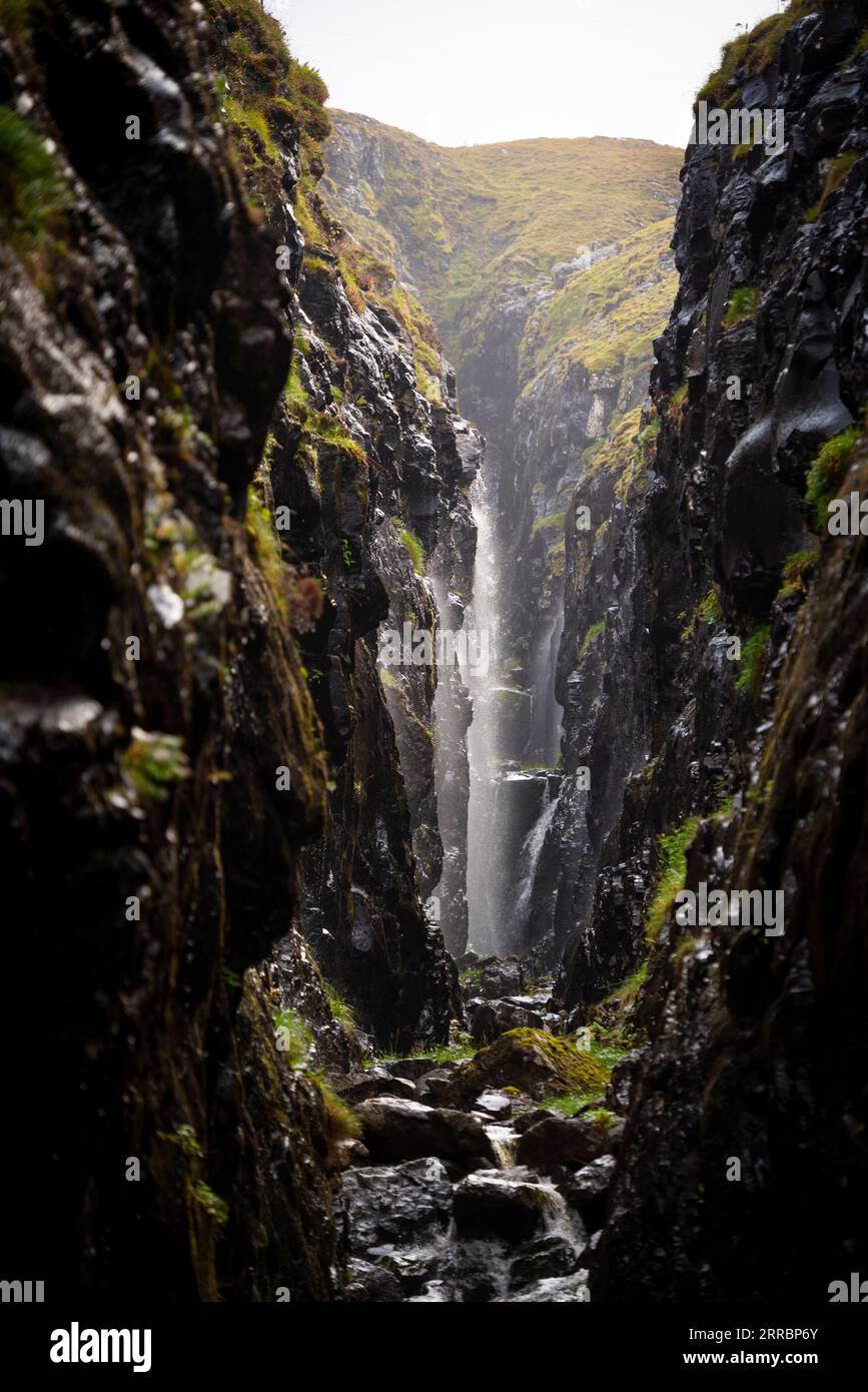 A rocky chasm wet with rain and mist from many small waterfalls glints ...