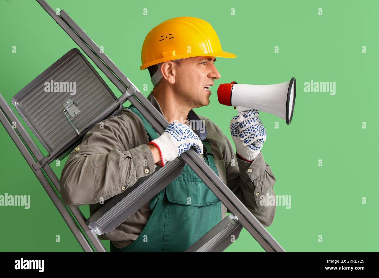 Mature builder with stepladder shouting into megaphone on green ...
