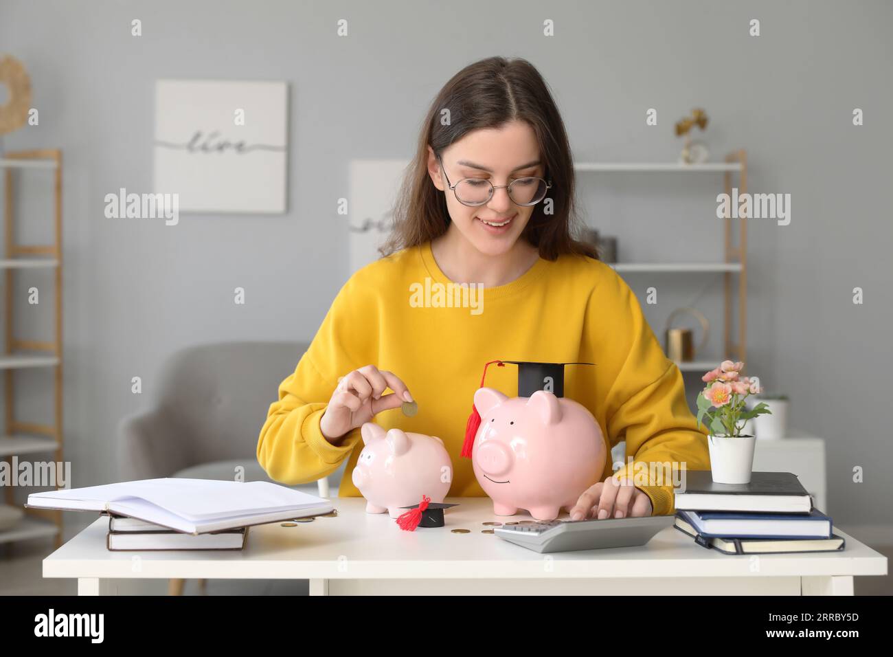 Happy female student calculating finances and putting coin in piggy ...