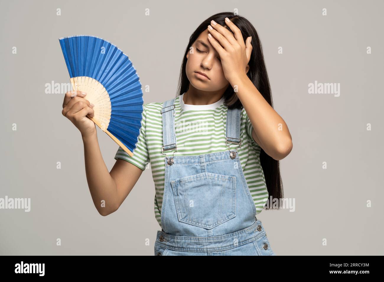 Sweaty teenage girl touching forehead using paper fan suffer from heat ...