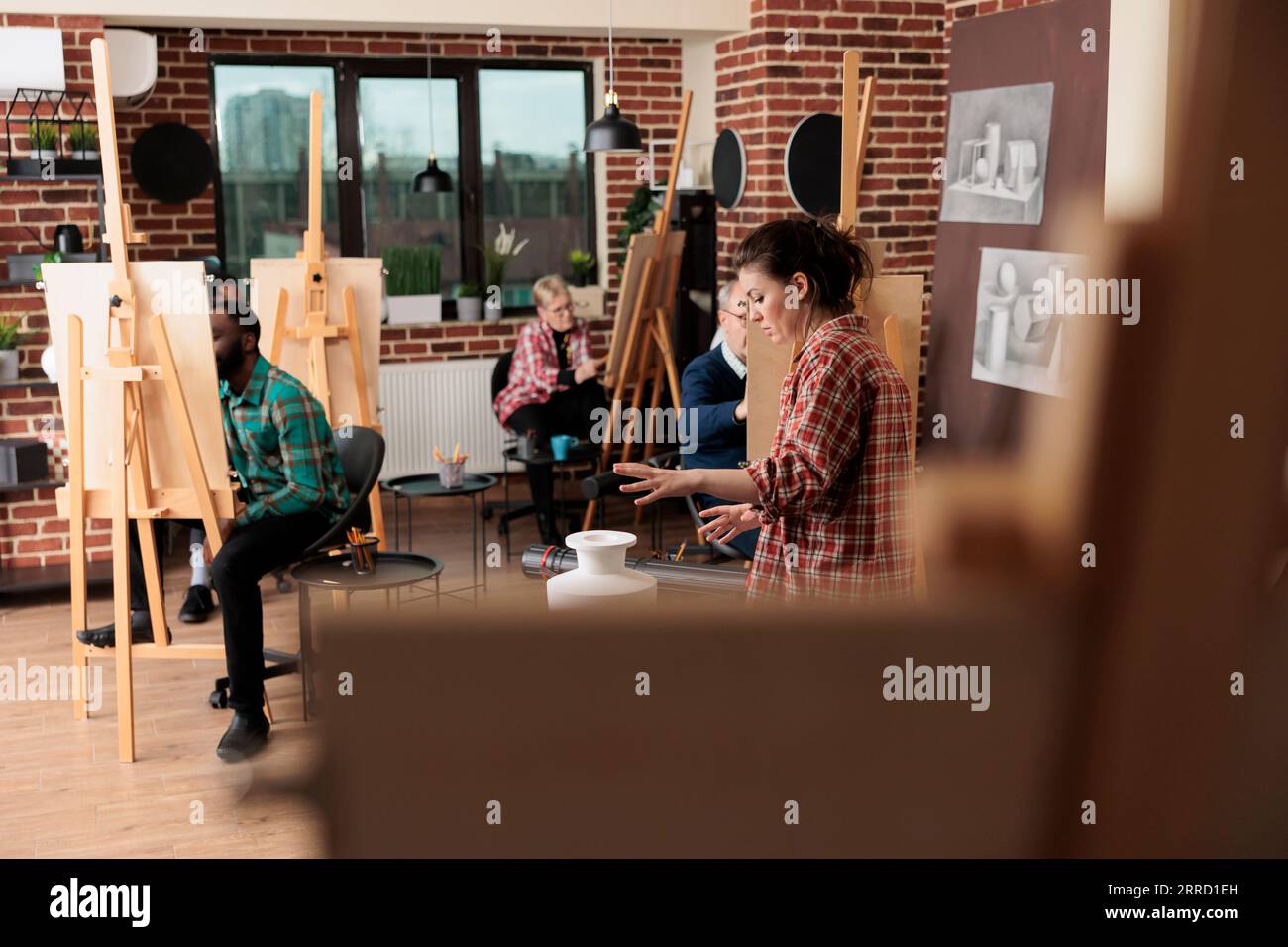 Group of different aged people sitting at easels studying drawing at ...
