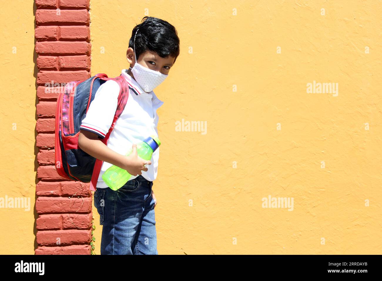 Latino boy with uniform shirt, mask, backpack, notebook and bottle of ...