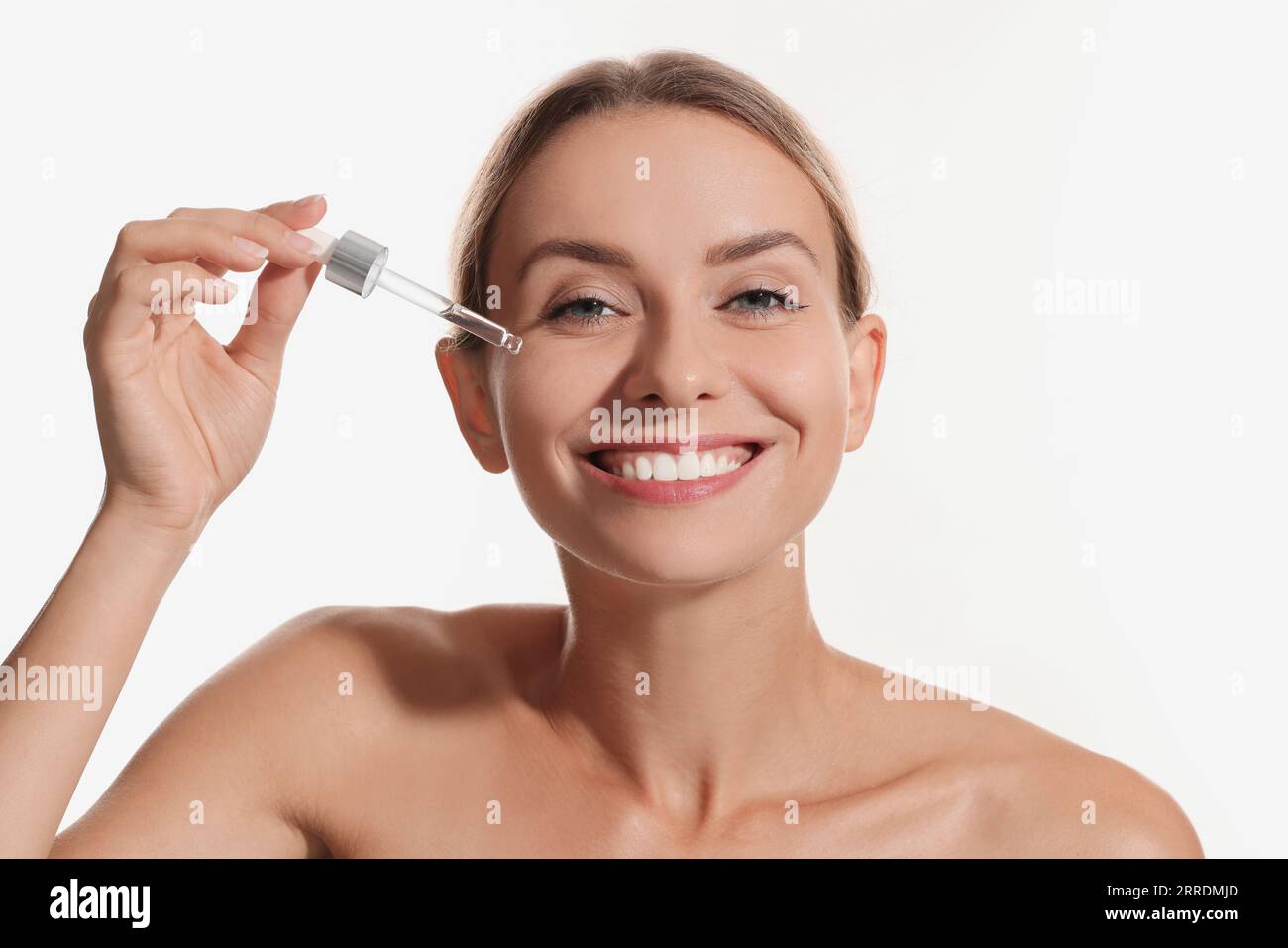 Beautiful woman applying cosmetic serum onto her face on white ...