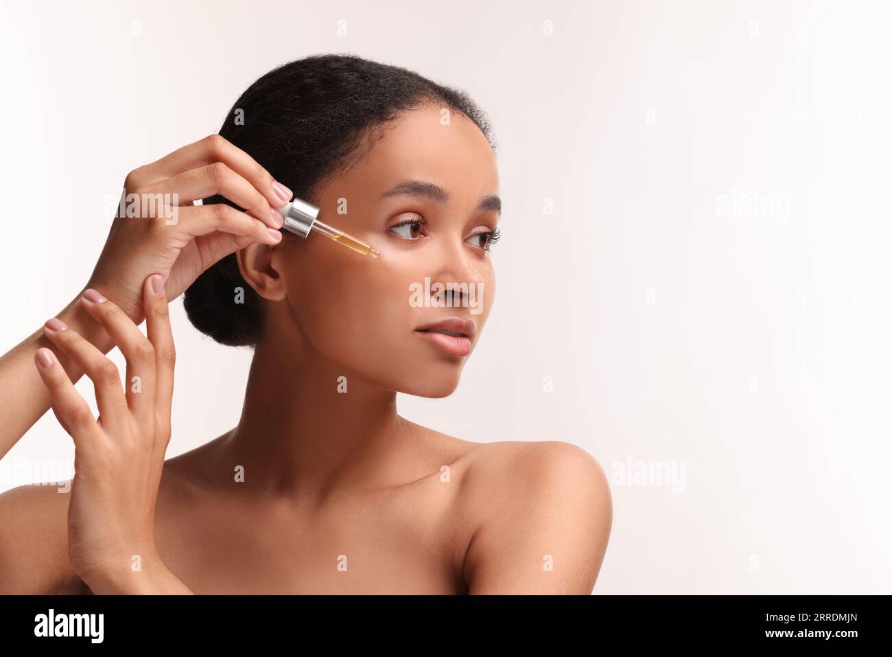 Beautiful woman applying serum onto her face on white background. Space ...