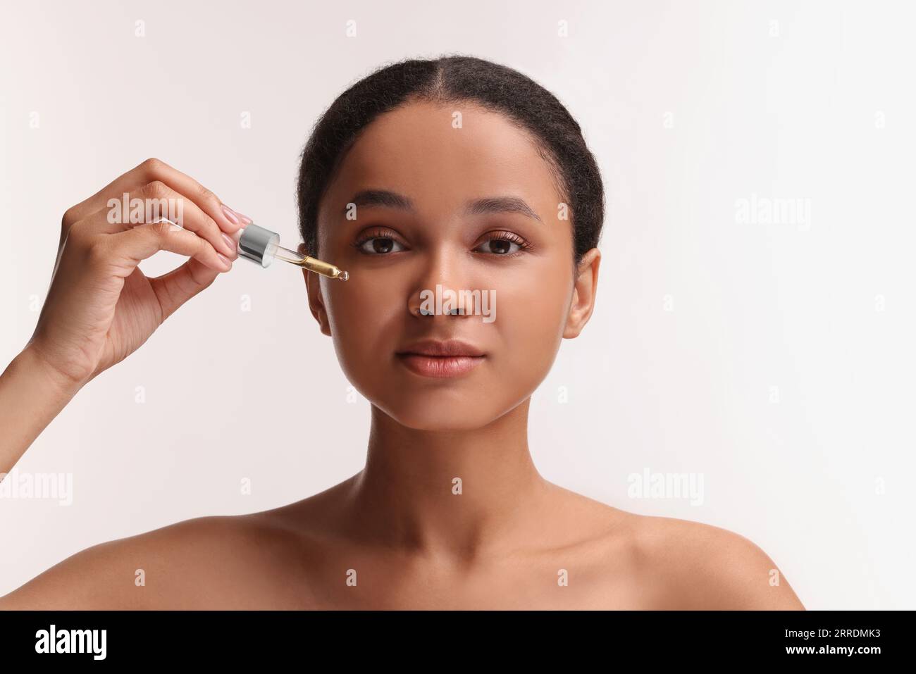 Beautiful woman applying serum onto her face on white background Stock ...