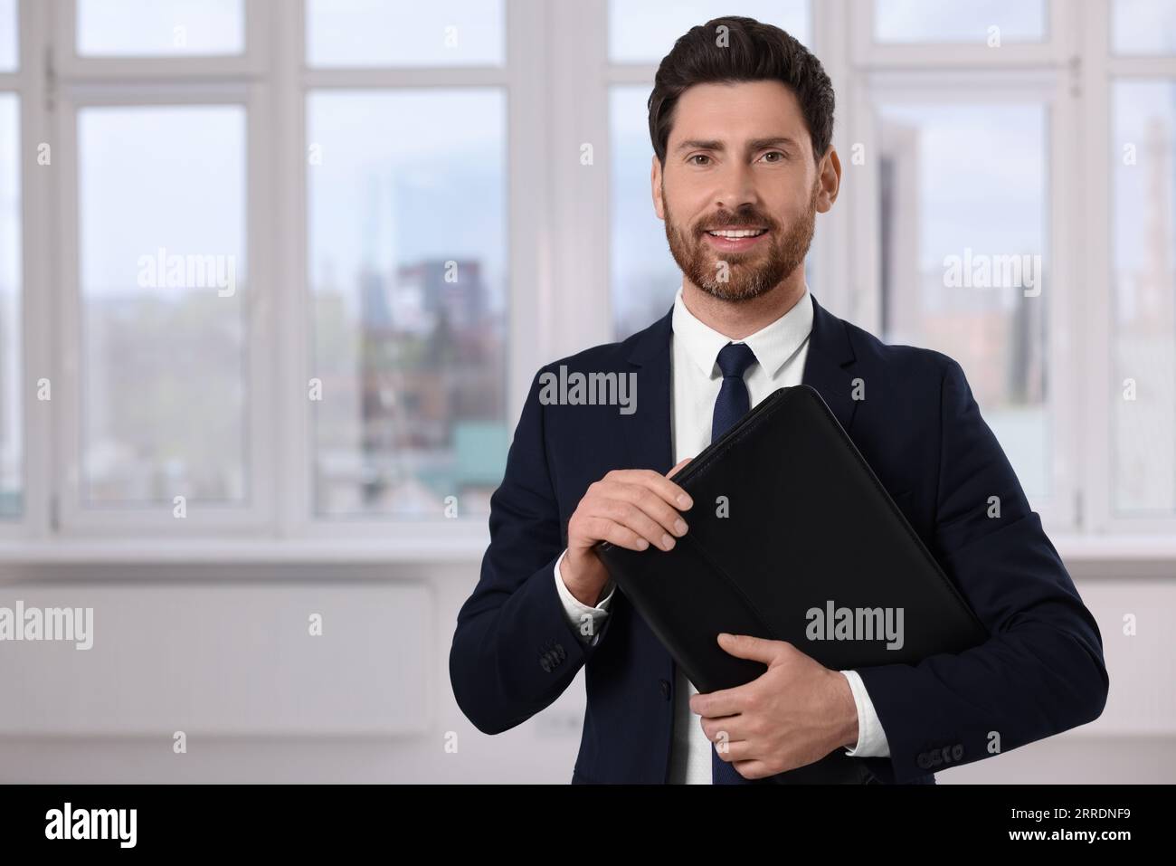 Happy real estate agent with leather portfolio indoors. Space for text ...
