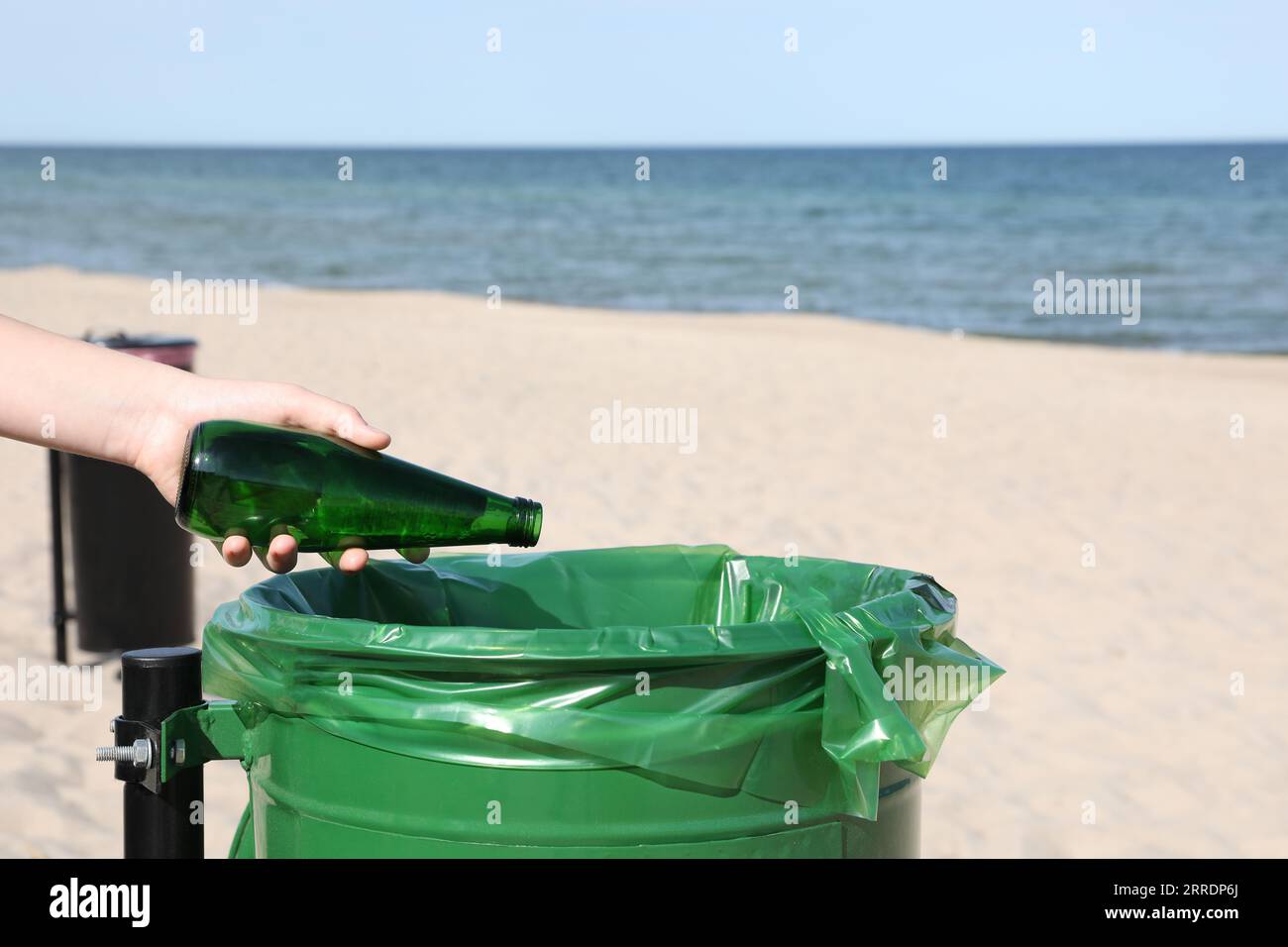 Woman throwing glass bottle in bin on beach, closeup. Recycling concept ...