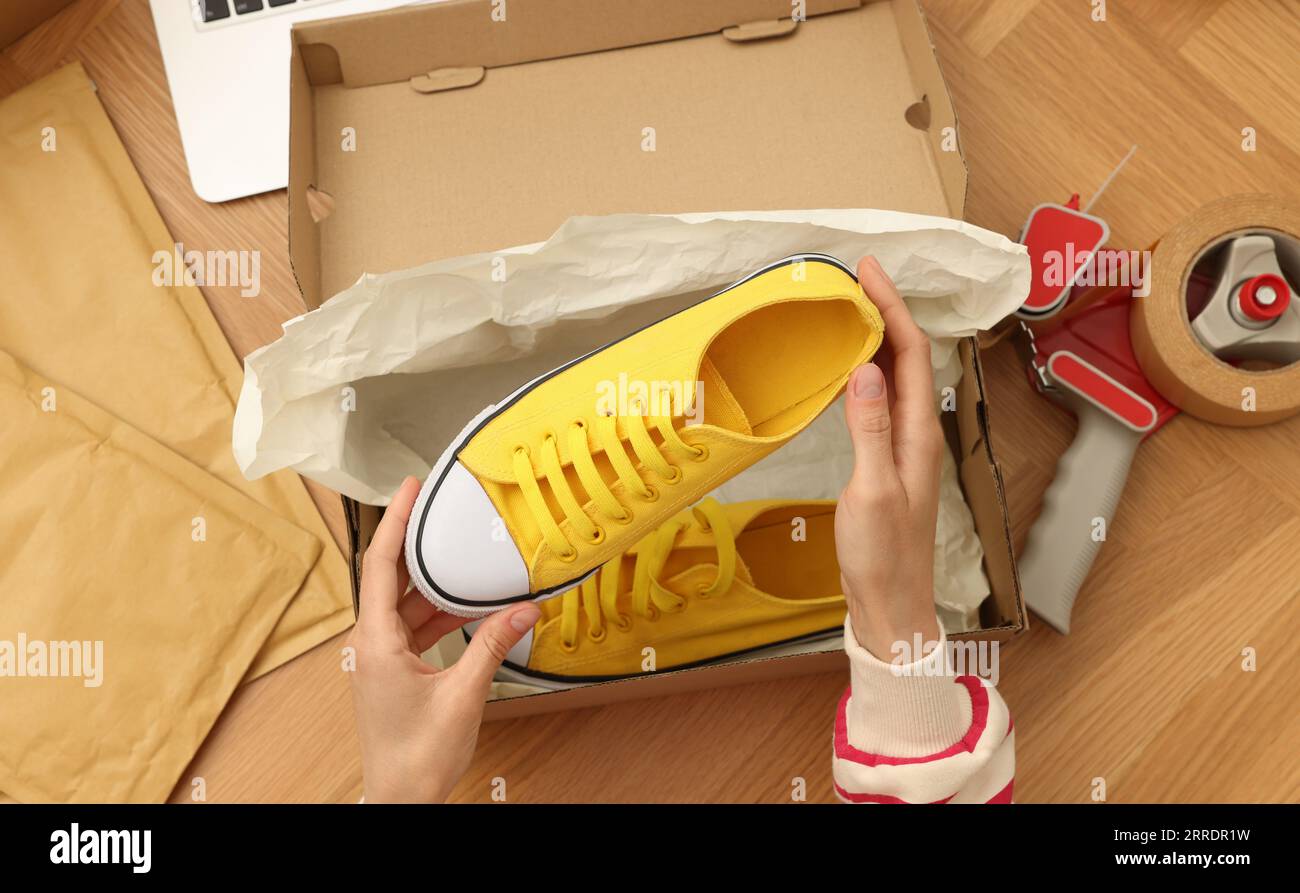 Woman packing sneakers into cardboard box at wooden table, top view ...