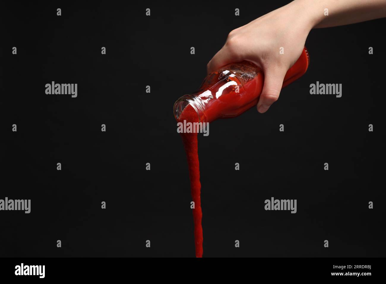 Woman pouring tasty ketchup from bottle on black background, closeup ...