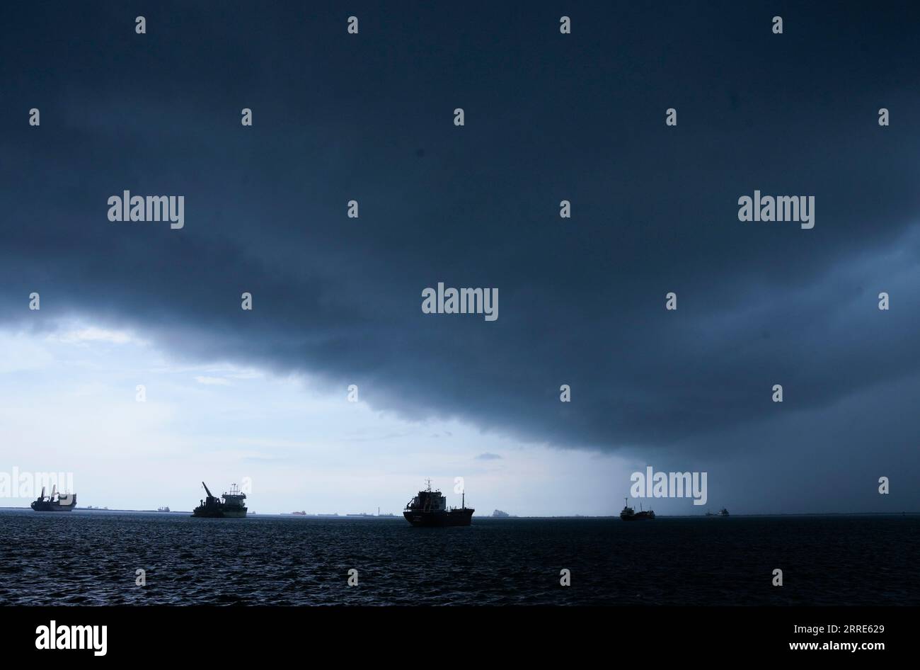 Storm clouds gather overhead as cargo ships that wait to transit ...