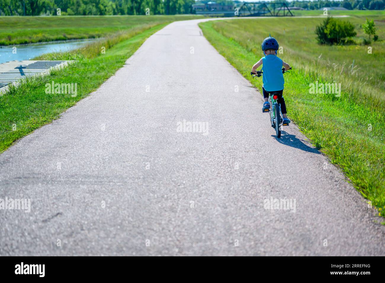 Caucasian boy wearing a helmet while riding a bike down a paved park ...