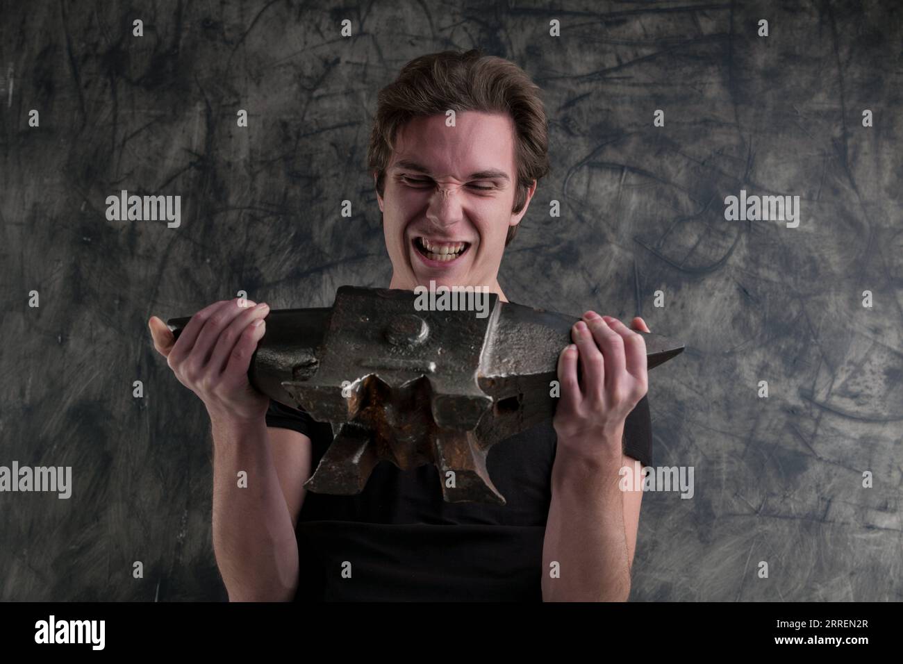 Against a stark grunge scene, a young male raises an anvil with visible ...